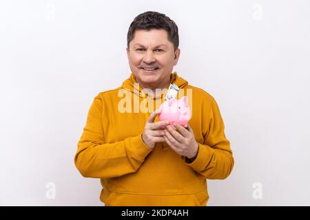 Middle-aged man holding piggy bank against blue background Stock Photo ...