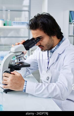 Young serious virologist in labcoat studying new bacteria or virus and ...