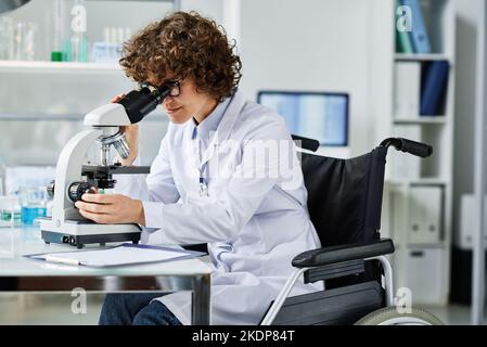 Young clinician with disability sitting on wheelchair by workplace in ...
