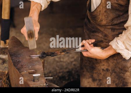 A blacksmith manually forges red-hot metal on an anvil with a hammer ...