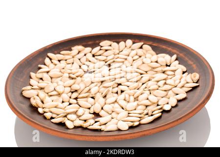 Unpeeled raw pumpkin seeds in a white ceramic saucer with a wooden ...