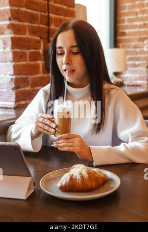 The brunette is working with a tablet at a table in a cafe. Drinks ...