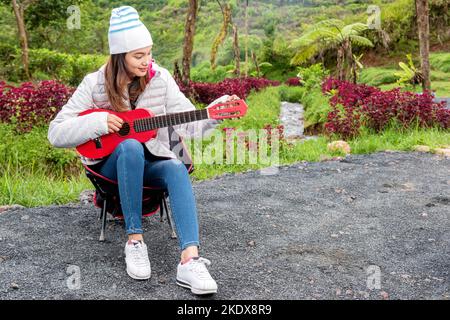 Asian woman playing guitar enjoying camp activity in nature Stock Photo ...
