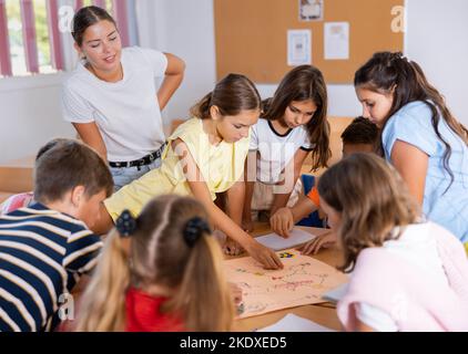 Schoolkids playing board game with teacher in classroom Stock Photo - Alamy