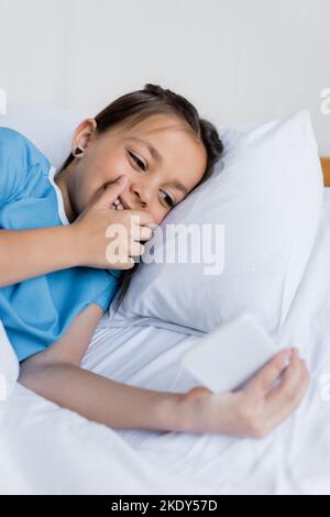 Kid in patient gown using blurred smartphone on hospital bed,stock ...