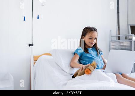 Kid in patient gown using blurred smartphone on hospital bed,stock ...