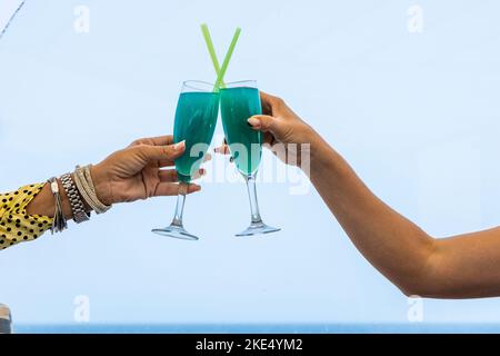 Two hands cheering with blue cocktails outdoors Stock Photo - Alamy