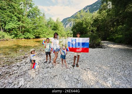 Four kids hold slovenian flags in rocky shore of a calm river in ...