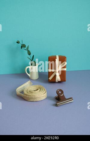 Gift box, ribbon roll, plant on purple table. blue background Stock ...