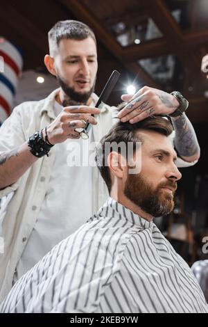 bearded brunette barber holding scissors in beauty salon,stock image ...