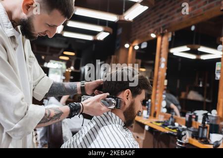 Side view of tattooed hairdresser holding comb and pointing at finger ...