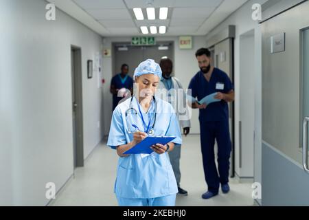 Biracial female doctor writing notes in busy hospital corridor, copy ...