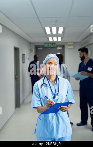 Biracial female doctor writing notes in busy hospital corridor, copy ...