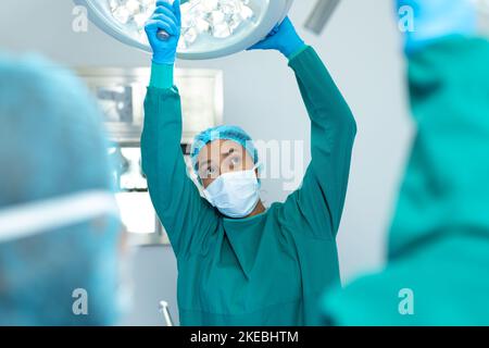 Biracial female surgeon adjusting lights in operating theatre for ...