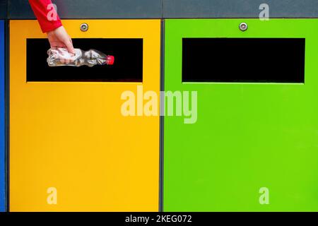 Hand throwing a plastic bottle into a colored garbage bin in the local ...