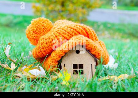 Chunky knitted hat put on a wooden cottage figurine placed on a green ...