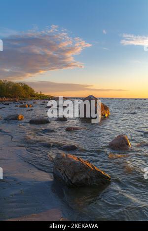 Rocky shore with stones sinking in the sea water. Sunset, orange light ...