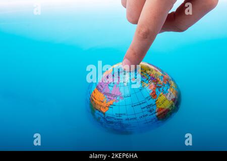 Little globe with finger on top floating in blue water Stock Photo - Alamy