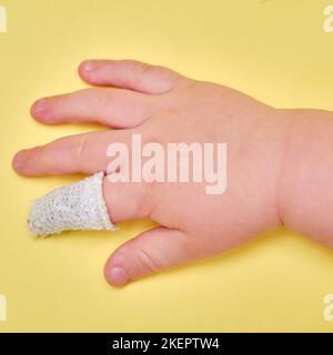 Baby s hand with a bandaged finger on a yellow studio background, close ...
