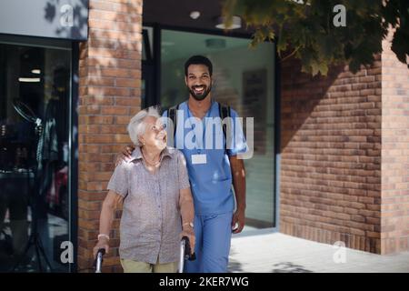 Caregiver walking with senior woman client in front of nurishing home ...