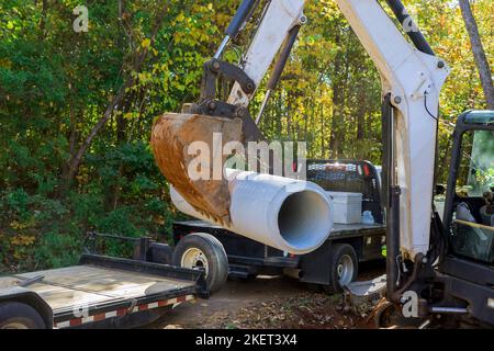 Worker use tractor lift up concrete sewage pipes from truck put down on ...