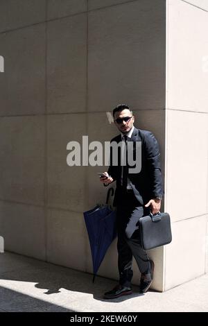 Elegant businessman leaning on wall in the city, using digital tablet ...