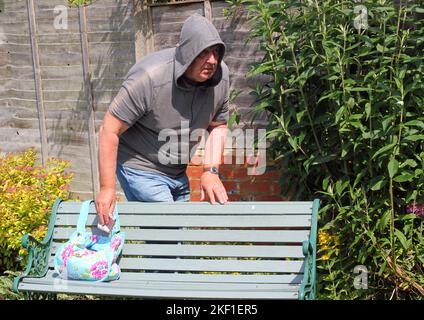 Thief leaning over a park bench and stealing property from a handbag ...