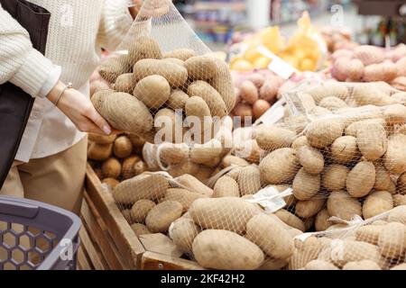 Woman puts mesh bag with potato into trolley for purchases in ...
