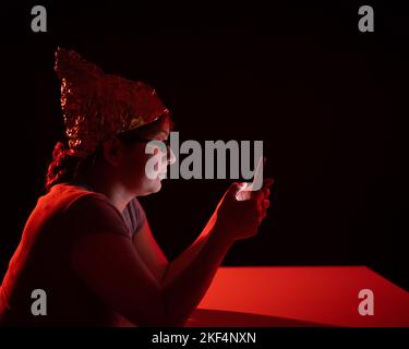 Paranoid caucasian woman using smartphone wearing tinfoil hat ...