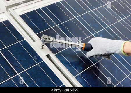A worker's hand screws solar panels onto a red tile roof with a torque ...