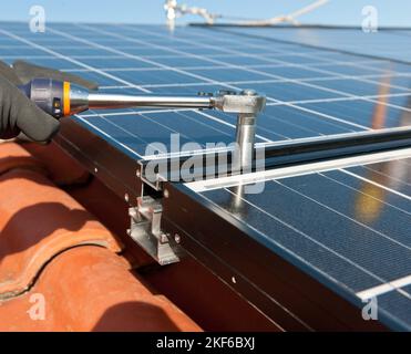 A worker's hand screws solar panels onto a roof with a torque wrench in ...