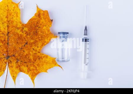 Autumn maple leaf and syringe with vaccine on white background ...