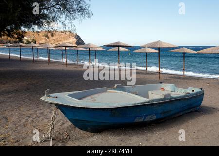 Boat pulled up ready for winter and straw sunshades on a deserted Greek ...