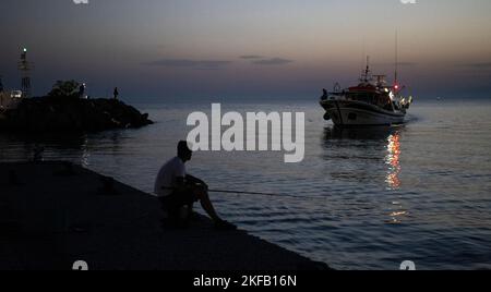 Fishermen stand on the shore and catches fish at sunset in the Aegean ...