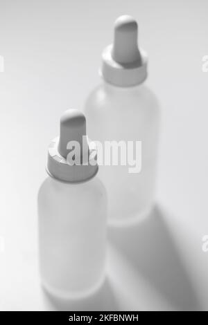 Two empty translucent glass dropper vials, one open. Different-sized bottles on white background ...
