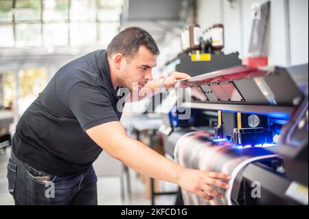 In the printing house, an experienced technician works on a UV printer ...
