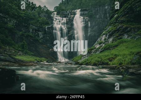 A long exposure shot of a Skjervefossen waterfall in a valley emerging ...