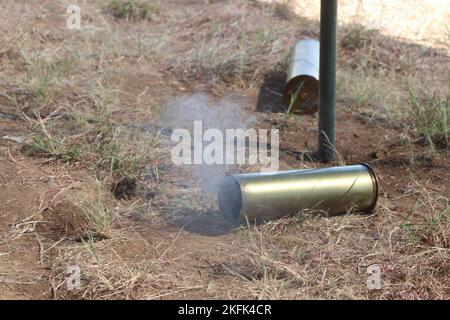 A smoking casing from a 105 mm howitzer round lands on the ground ...