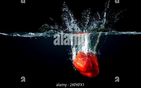 Red pepper in water with splashes on black background Stock Photo - Alamy