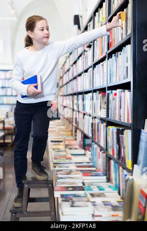 Girl, portrait and books on ladder in library of home with smile for ...