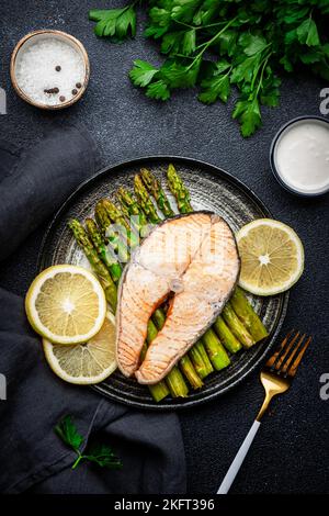 Baked steam salmon with asparagus and lemon on plate. White table ...