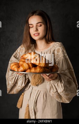 Ukrainian woman in national dress holds a tray with rosy croissants on ...