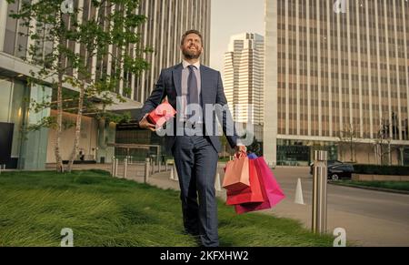 laughing man in formalwear with shopping bags and present box walk ...