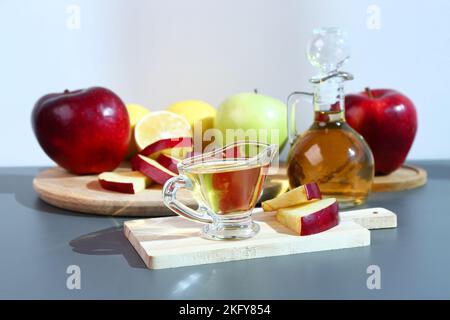 Wooden board with gravy boat of apple cider vinegar and fruits on pink ...