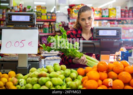 Smiling european female seller weighing celery Stock Photo - Alamy