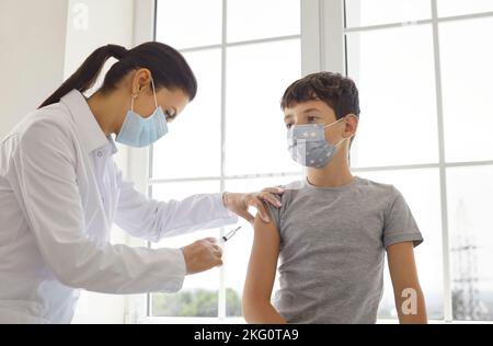 Doctor is giving a vaccine injection to teen girl in shoulder in clinic ...