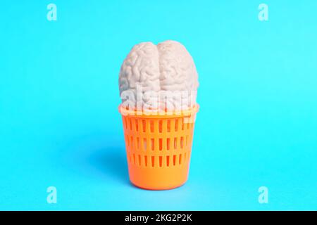 Human brain in a trash bin and toy home cleaning tools arranged on blue ...