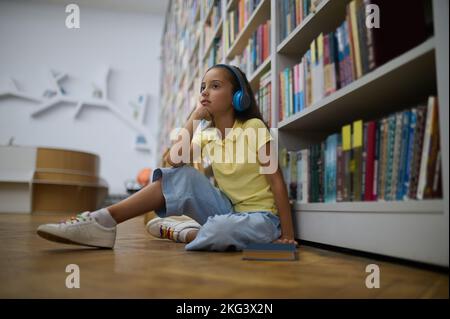 Girl in yellow tshirt sitting on floor in the library and listening to ...