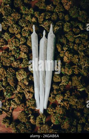 Close-up of three cannabis joint with chopped marijuana on wooden table ...