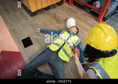 Unconscious Asian warehouse male worker getting first aid by his female ...